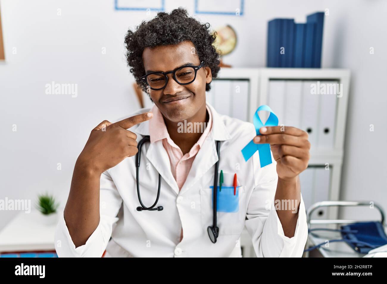 African doctor man holding blue ribbon pointing finger to one self ...