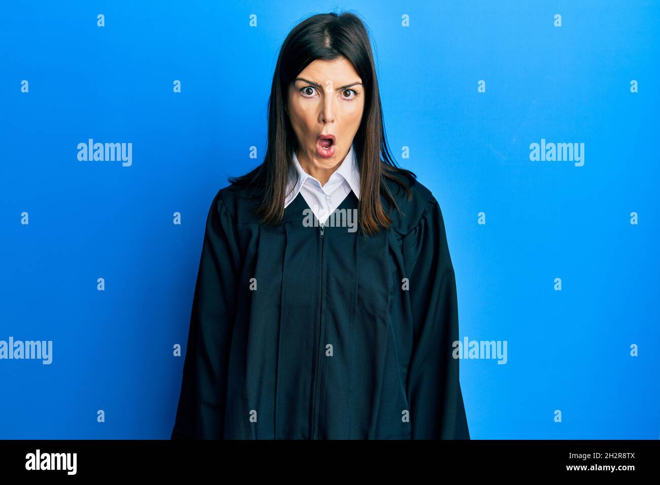 Young hispanic woman wearing judge uniform afraid and shocked with ...