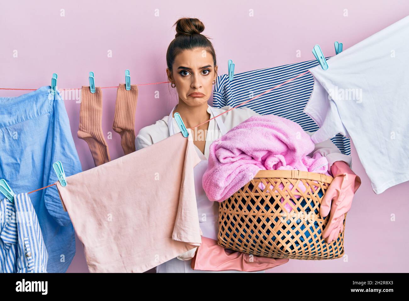 Beautiful brunette young woman holding laundry basket depressed and worry for distress, crying ...