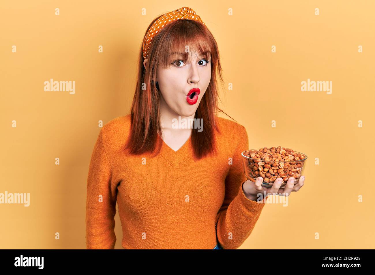 Redhead young woman holding peanuts scared and amazed with open mouth ...