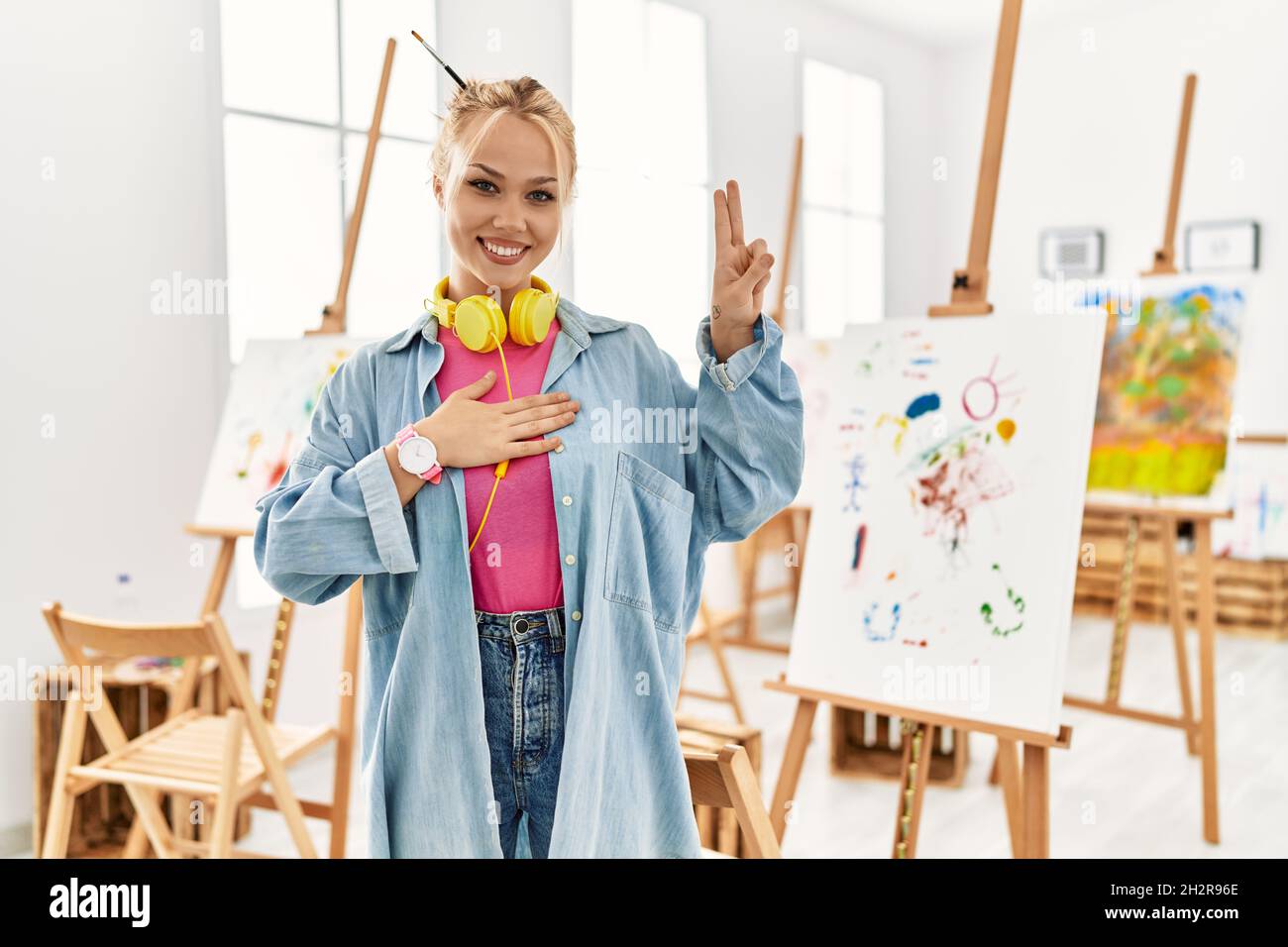 Young caucasian girl at art studio smiling swearing with hand on chest ...