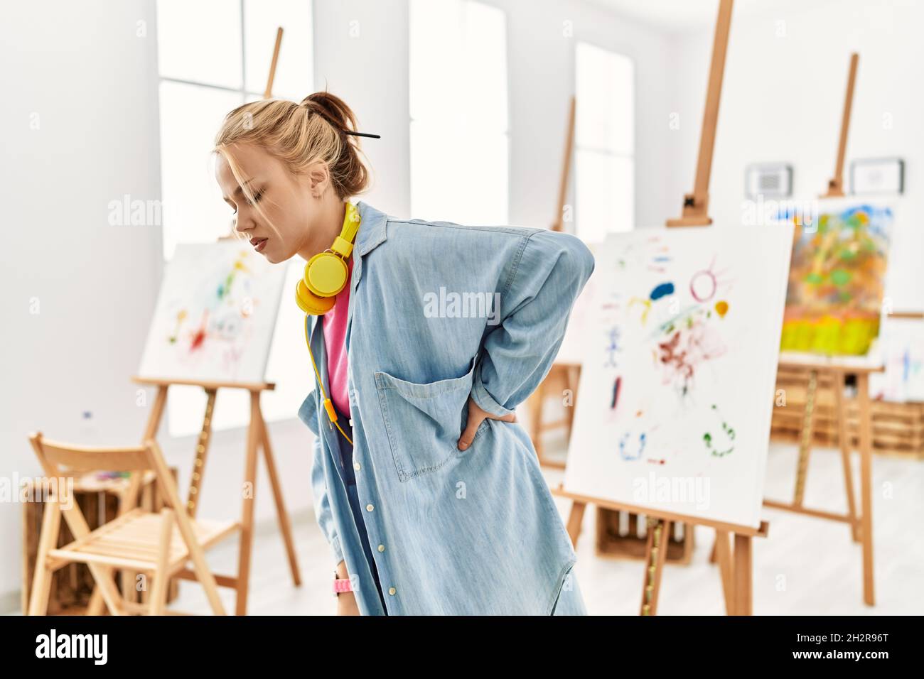 Young caucasian girl at art studio suffering of backache, touching back ...