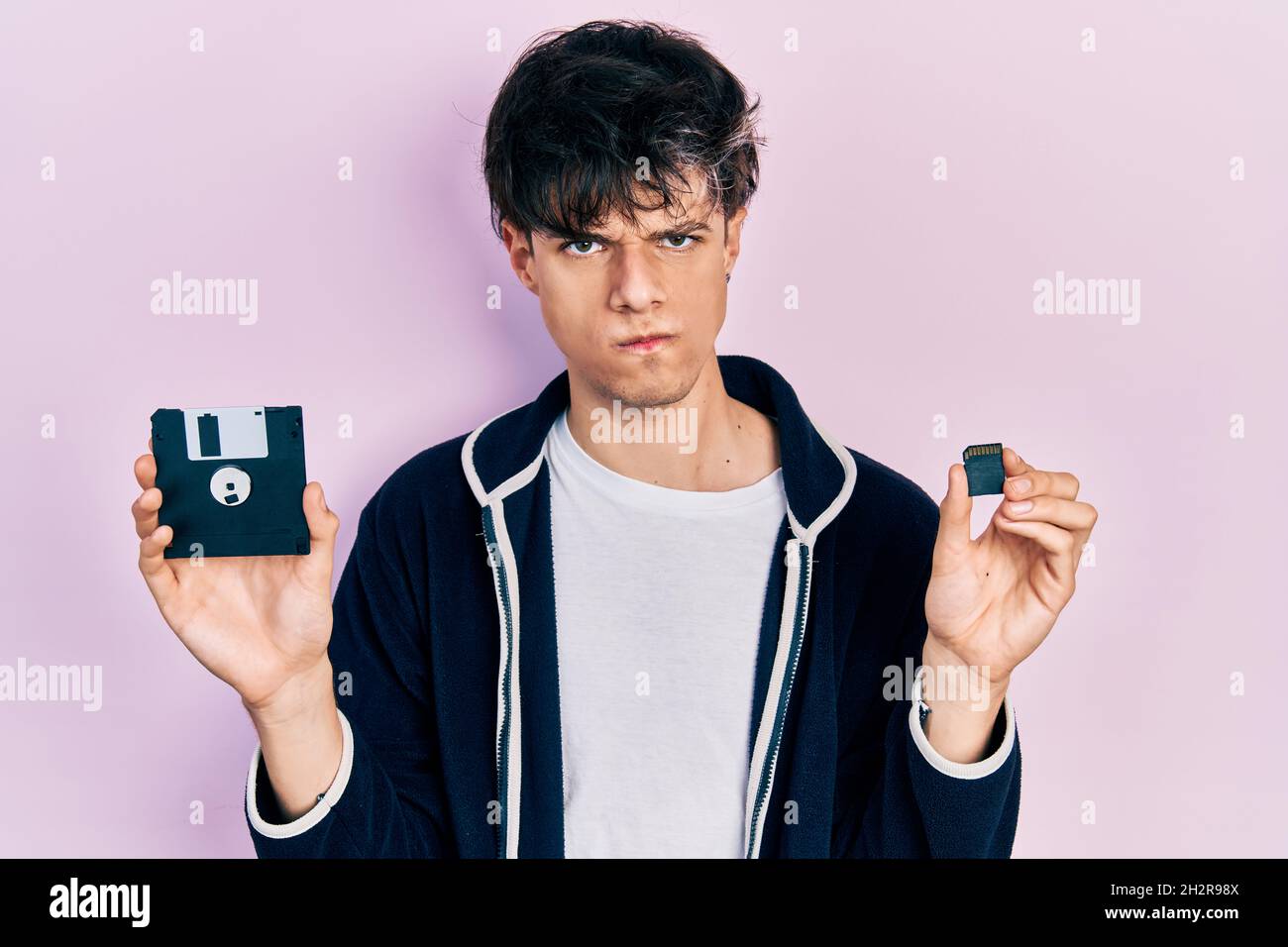 Handsome hipster young man holding floppy disk and sdxc card skeptic ...
