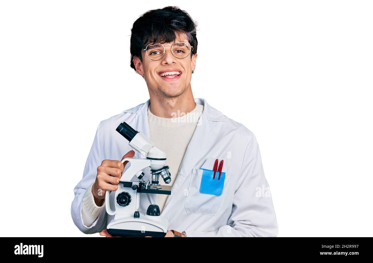 Handsome hipster young man wearing lab coat holding microscope smiling ...
