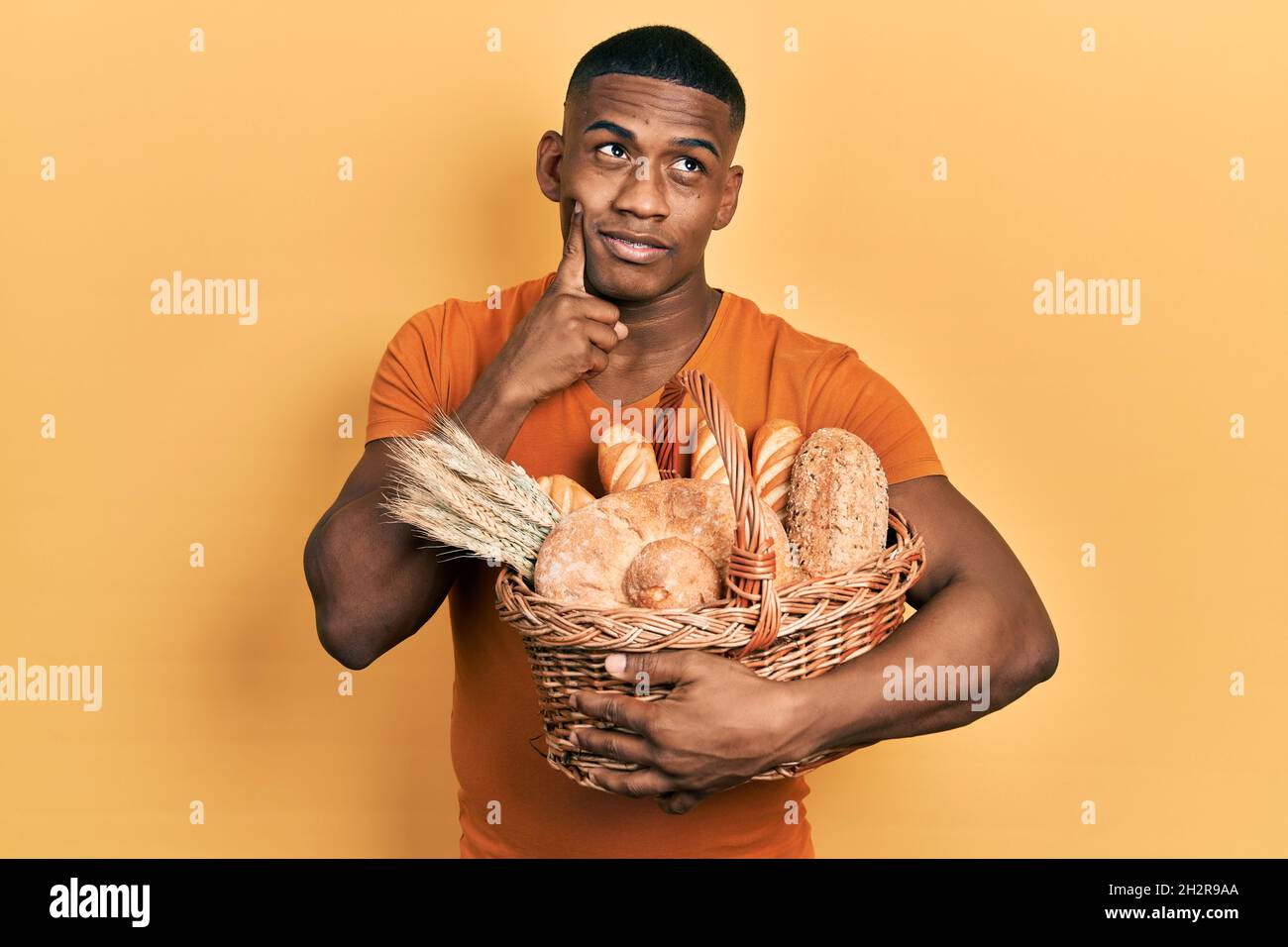 Young black man holding wicker basket with bread serious face thinking ...