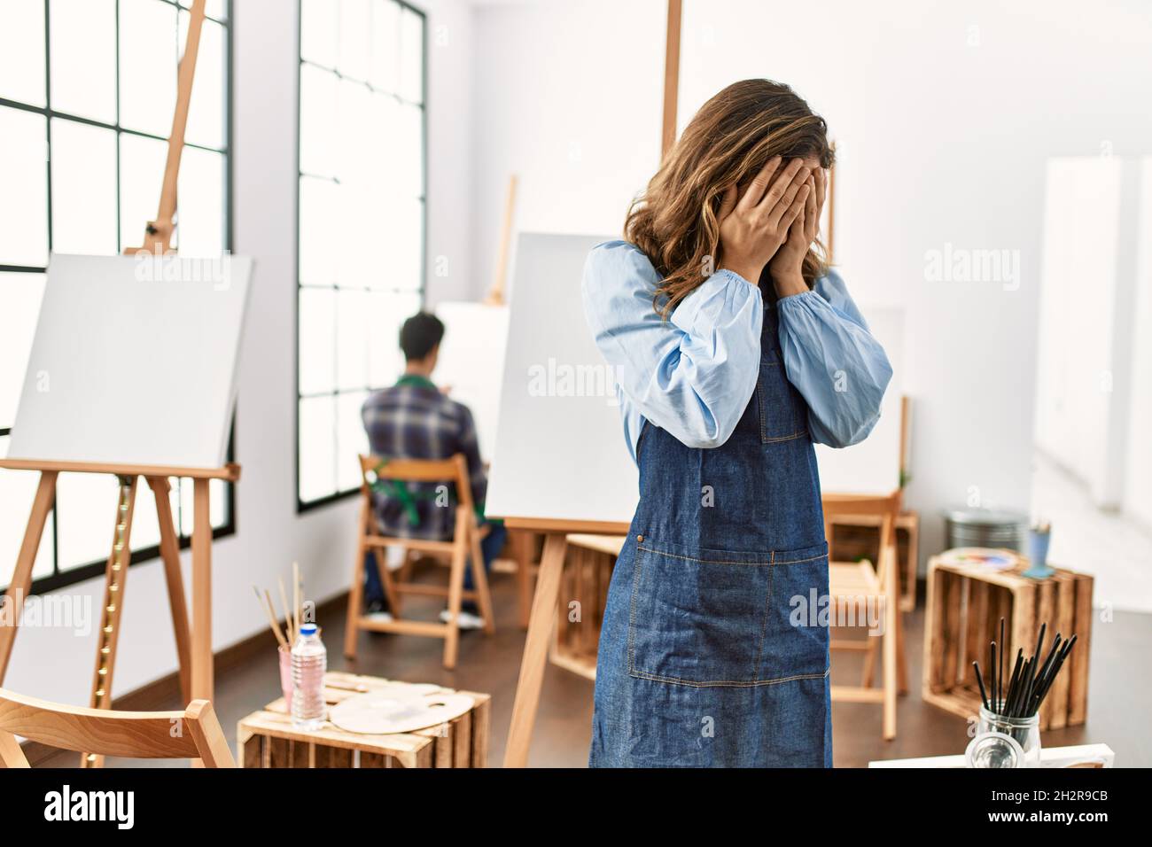 Young artist woman at art studio with sad expression covering face with ...