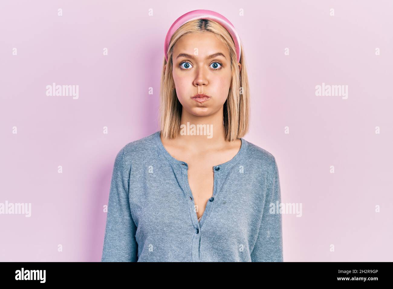 Beautiful blonde woman standing over pink background puffing cheeks ...