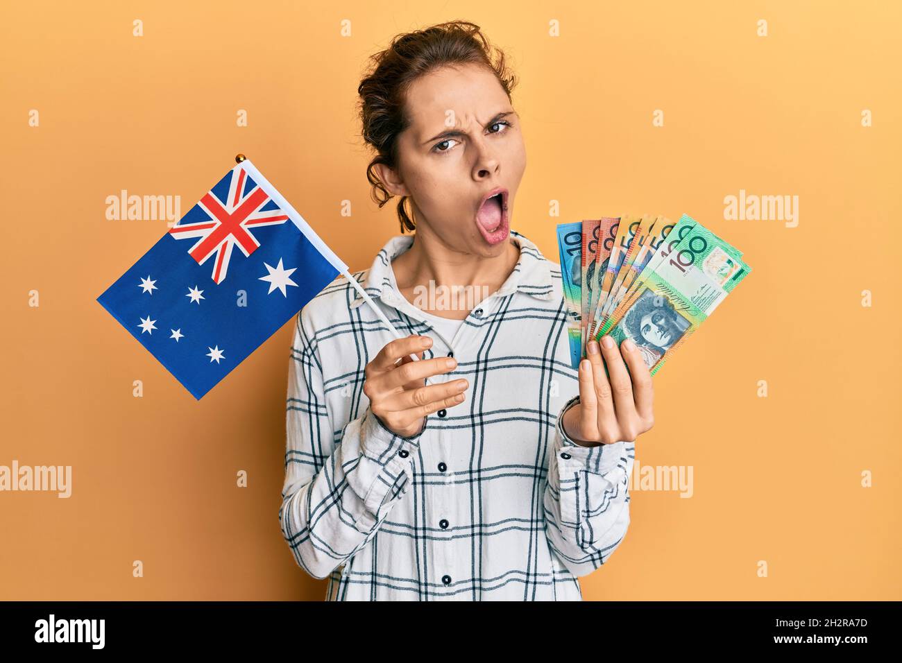Young brunette woman holding australian flag and dollars in shock face ...