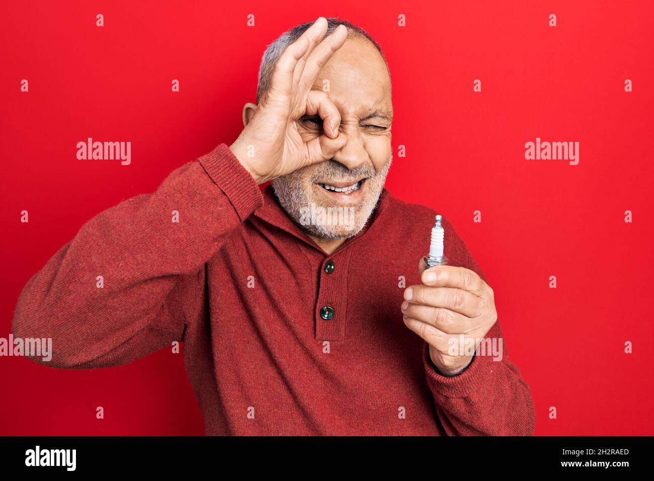 Handsome mature man holding spark plug smiling happy doing ok sign with ...