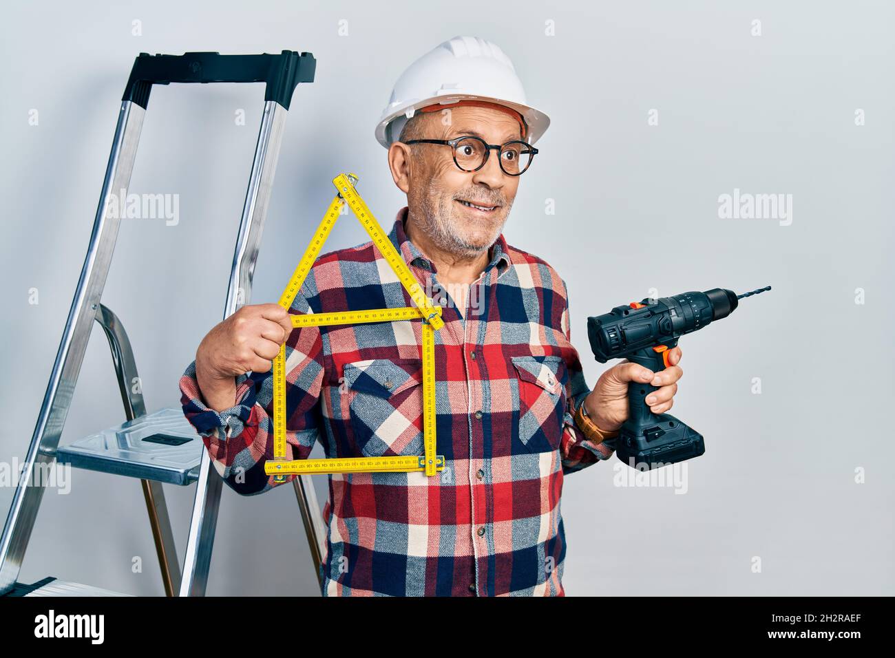 Handsome mature handyman holding screwdriver wearing hardhat by ...