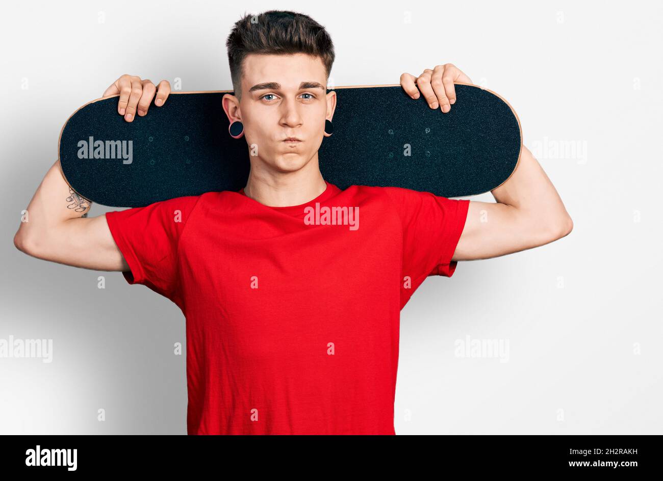 Young caucasian boy with ears dilation holding skate over shoulders ...
