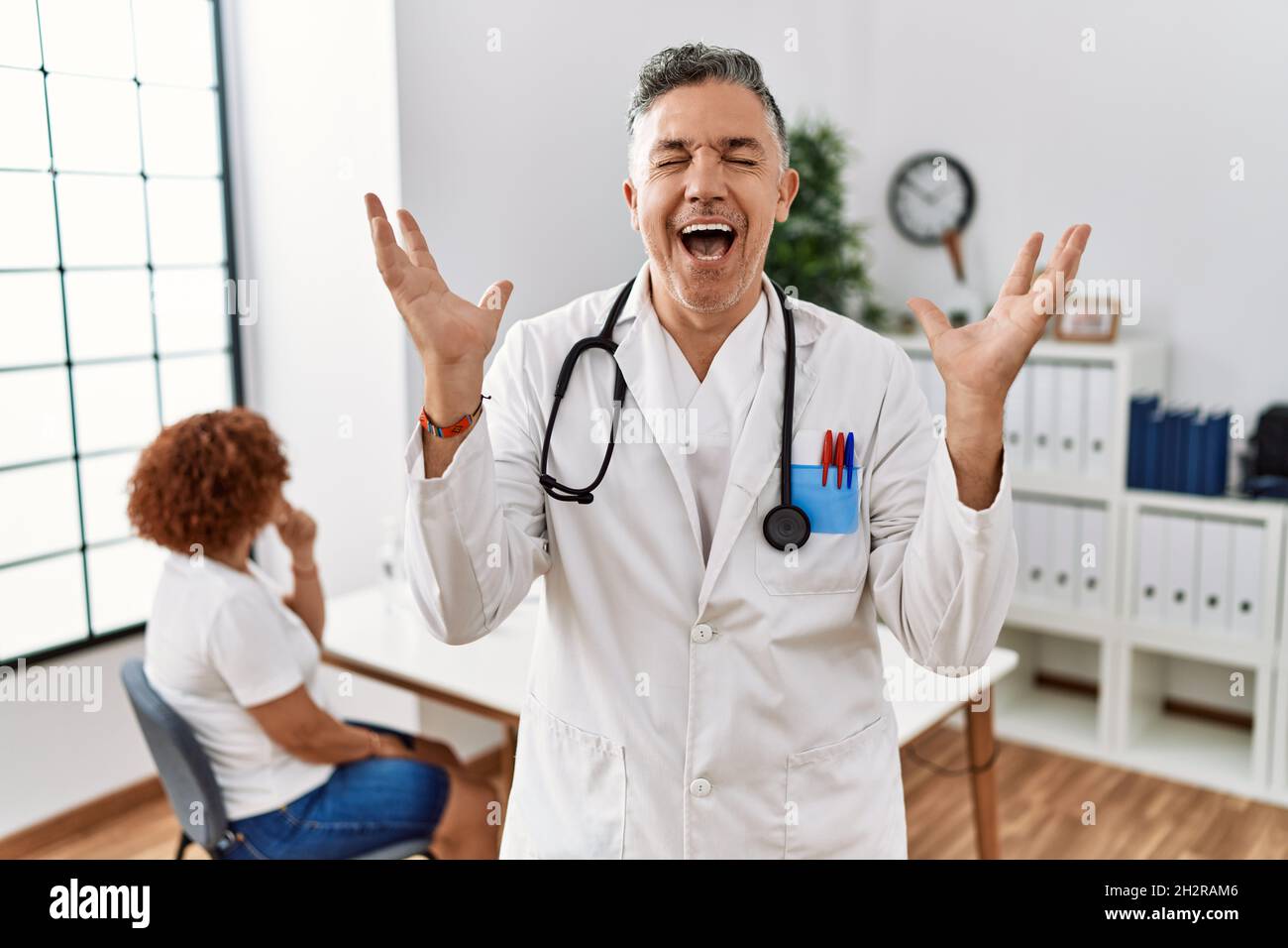 Middle age doctor man at the clinic with a patient celebrating mad and ...