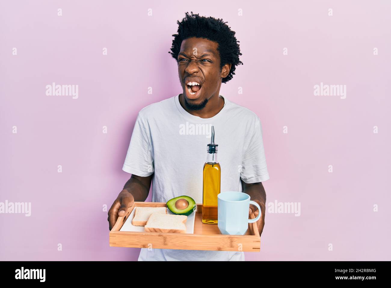 Young african american man holding tray with breakfast food angry and ...