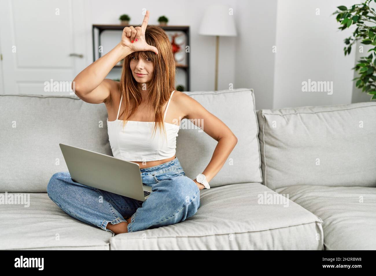 Hispanic woman sitting on the sofa at home using laptop making fun of ...