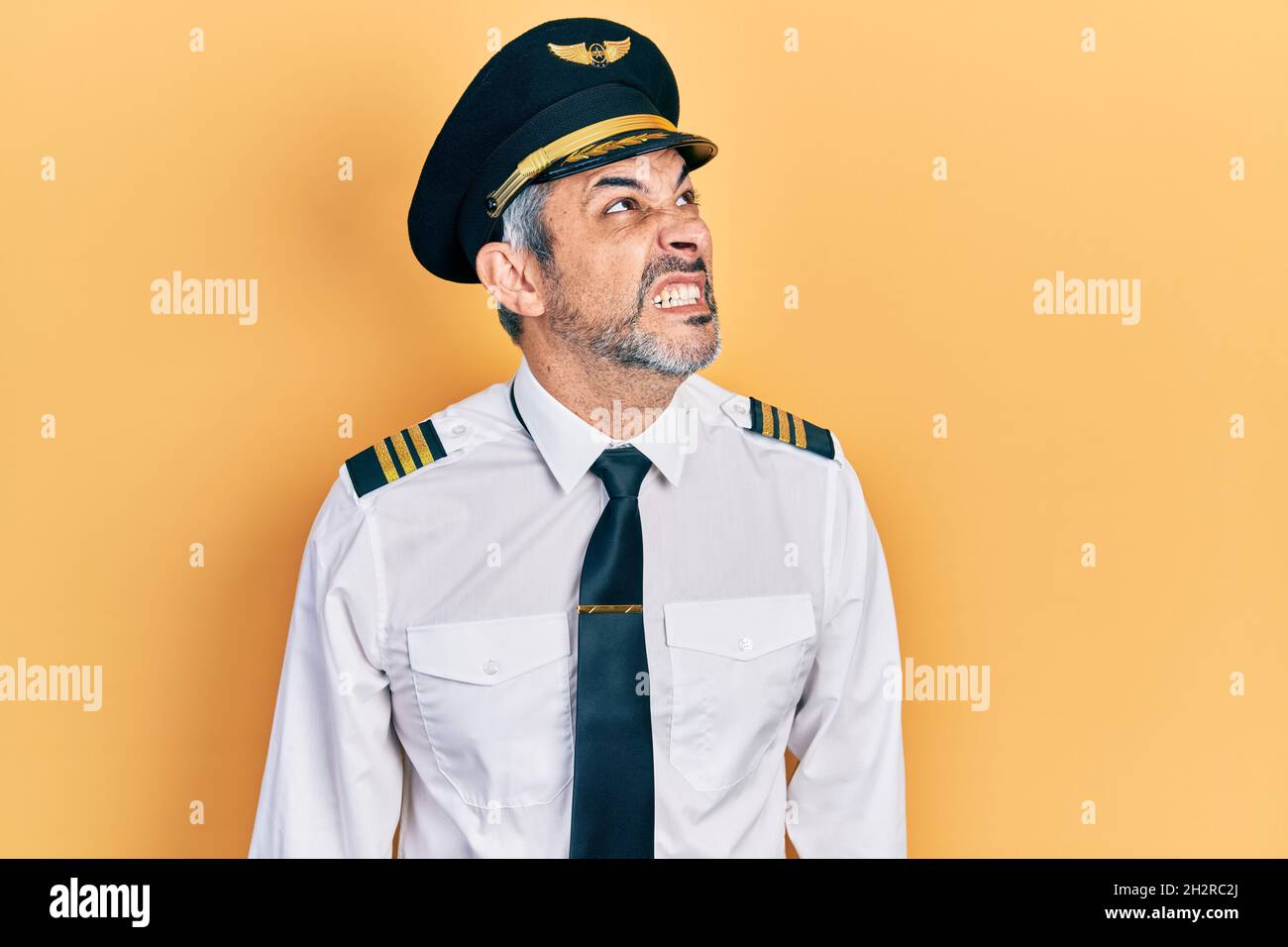 Handsome middle age man with grey hair wearing airplane pilot uniform angry and mad screaming ...
