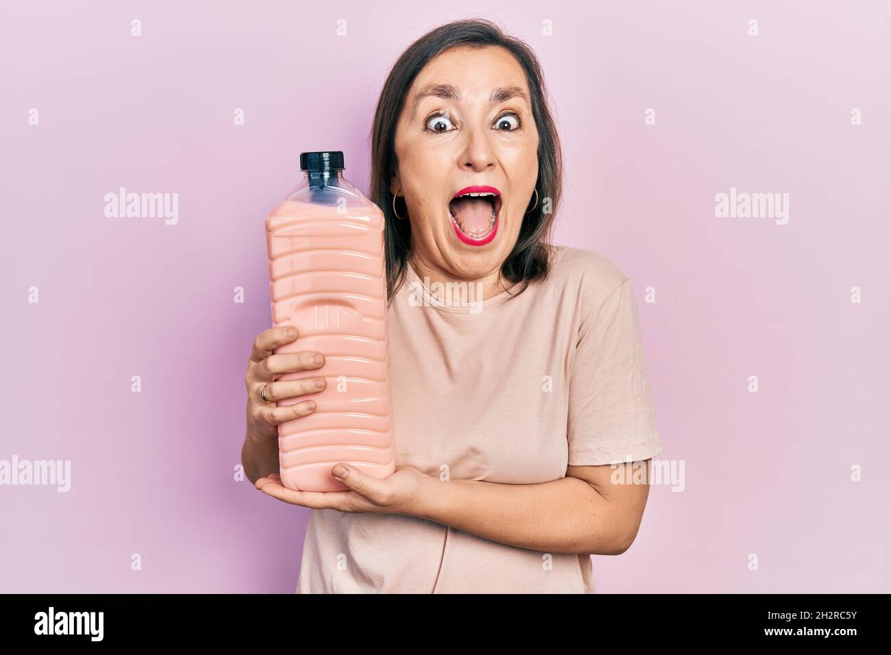 Middle age hispanic woman holding detergent bottle celebrating crazy and amazed for success with ...
