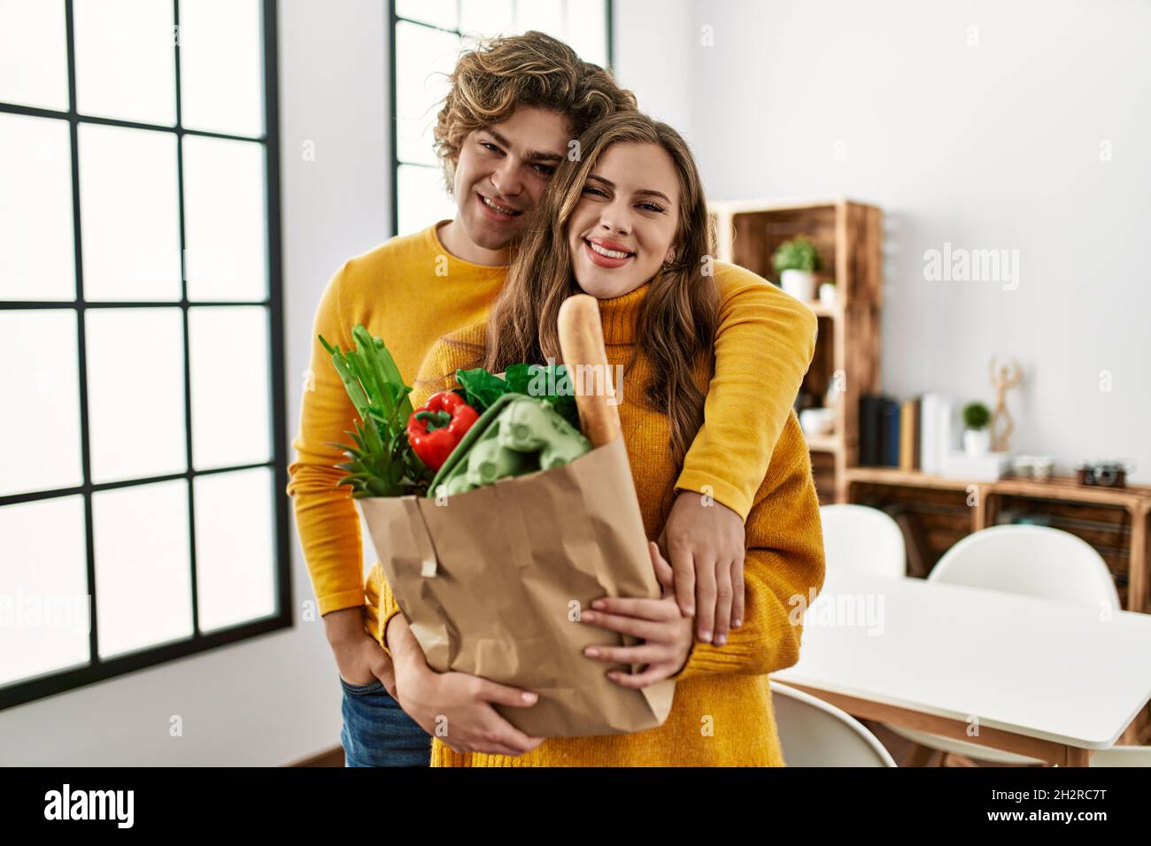 Young caucasian couple holding groceries paper bag hugging each other ...