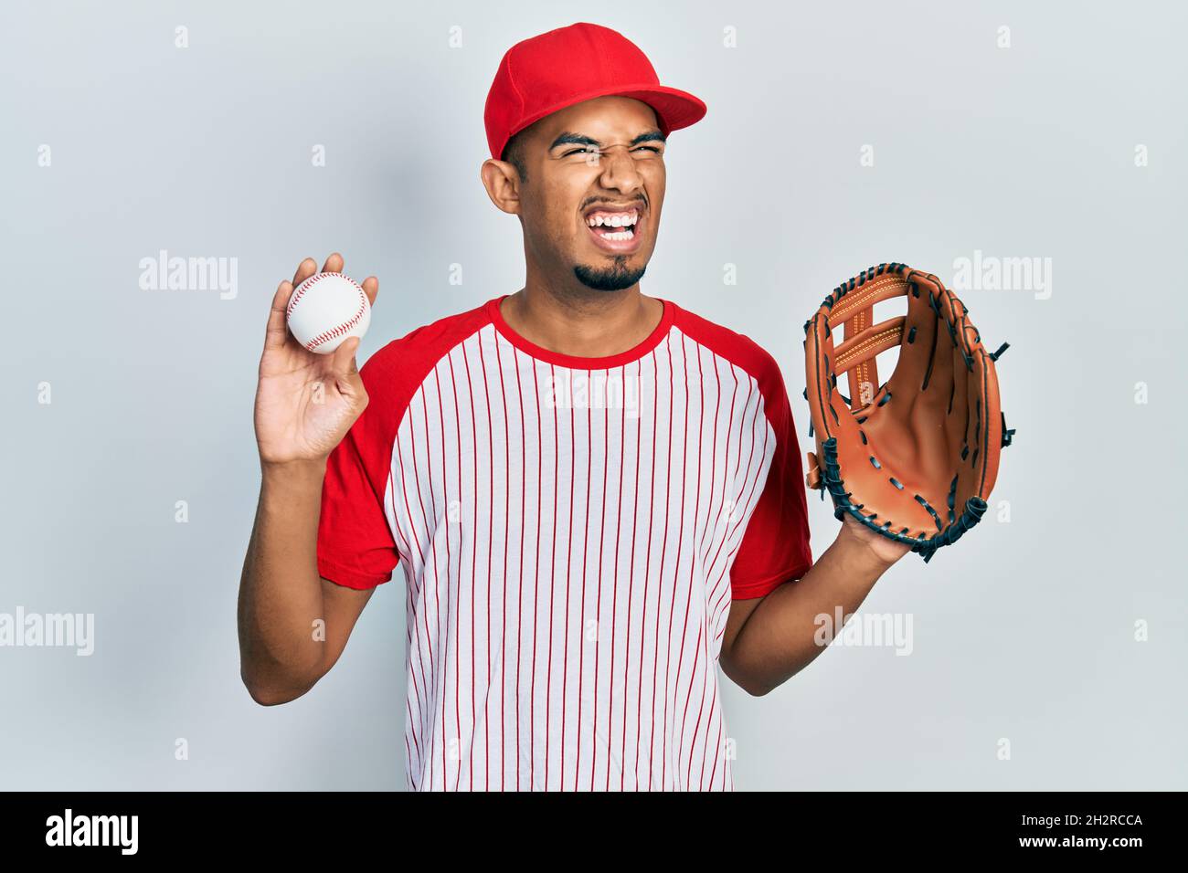 Young african american man wearing baseball uniform holding glove and ...