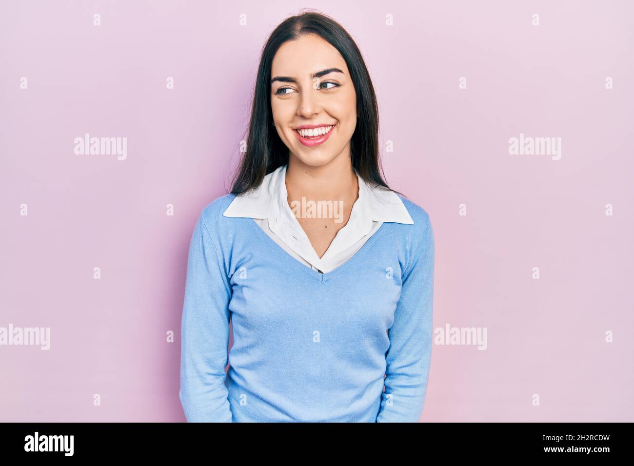 Beautiful woman with blue eyes standing over pink background looking ...