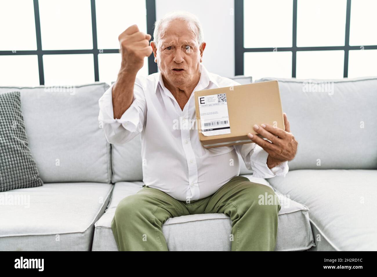 Senior man holding delivery package at home annoyed and frustrated ...