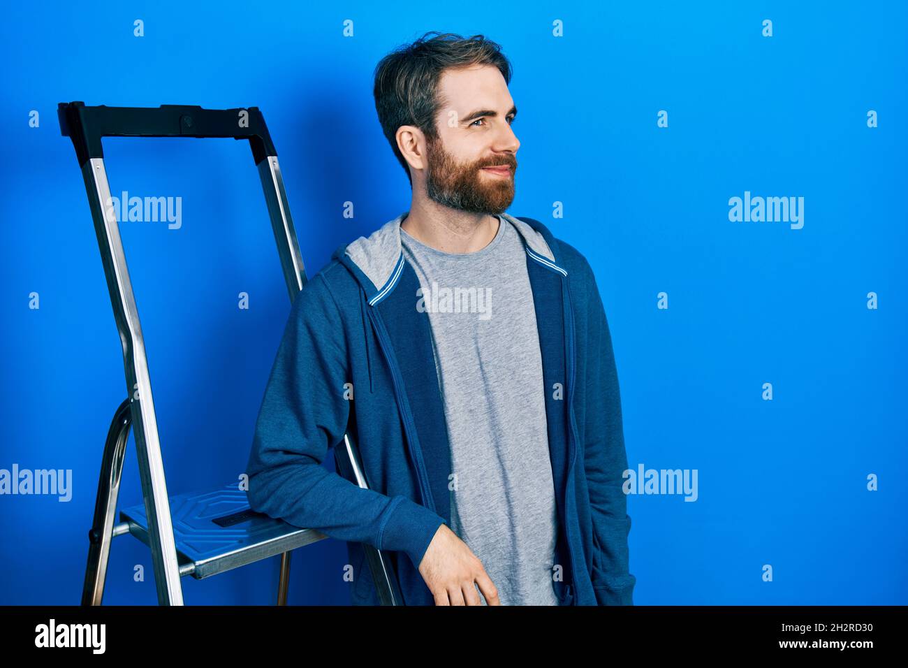 Caucasian man with beard by ladder looking away to side with smile on ...