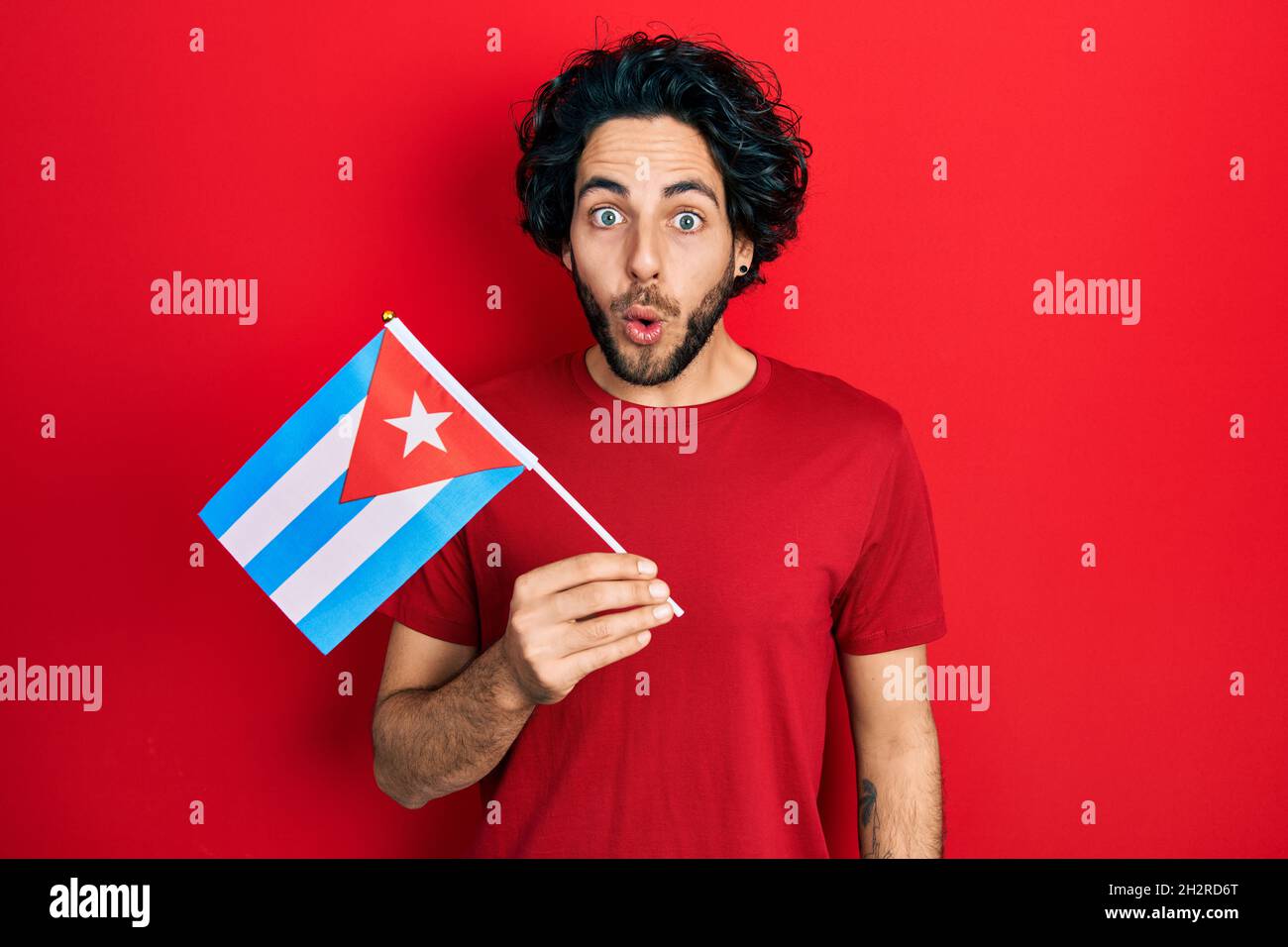 Handsome hispanic man holding cuba flag scared and amazed with open ...