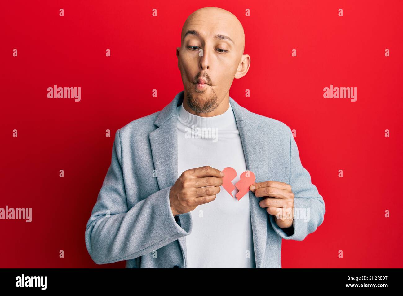 Bald man with beard holding broken heart paper shape making fish face ...