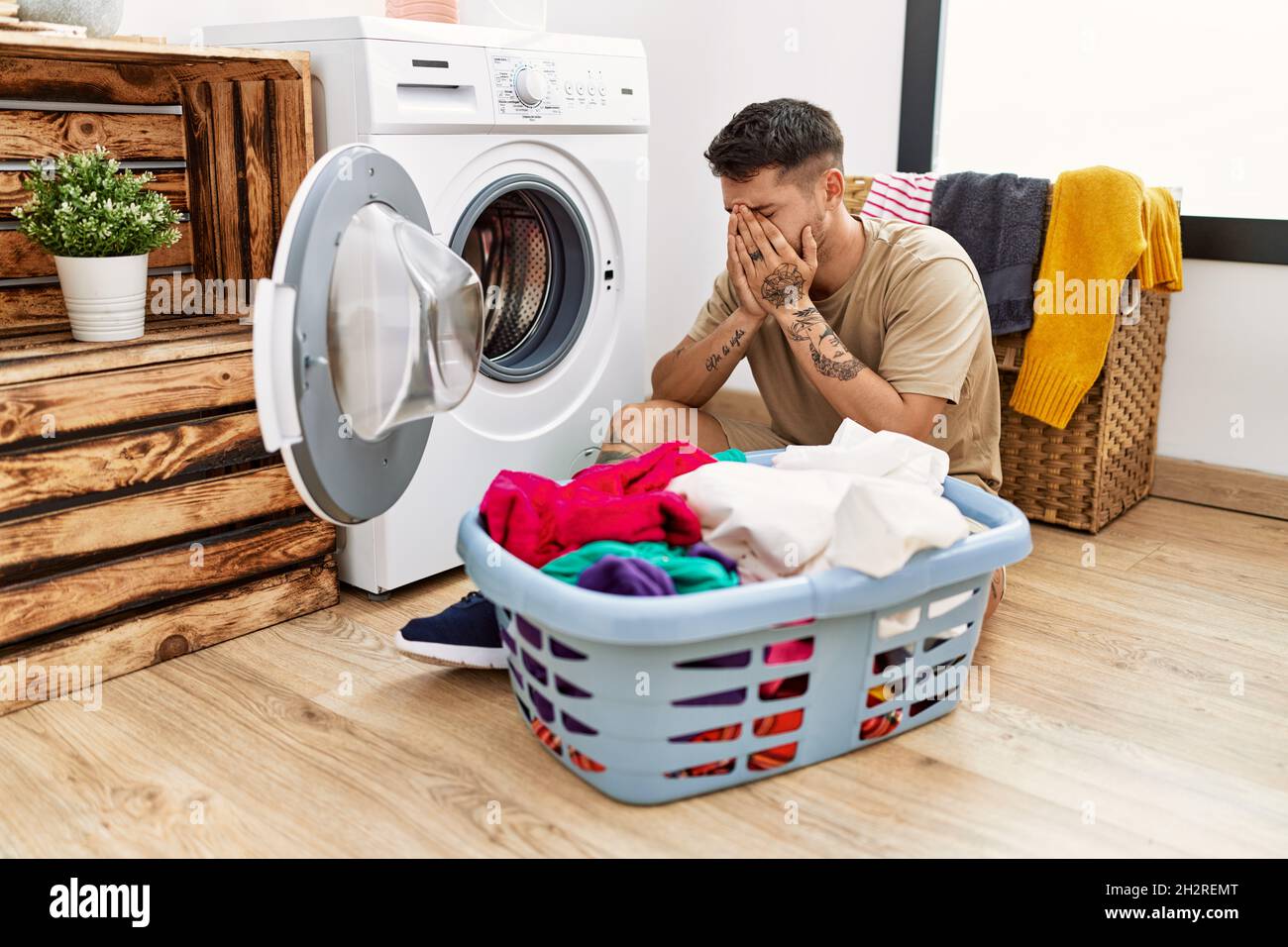 Young handsome man putting dirty laundry into washing machine with sad ...
