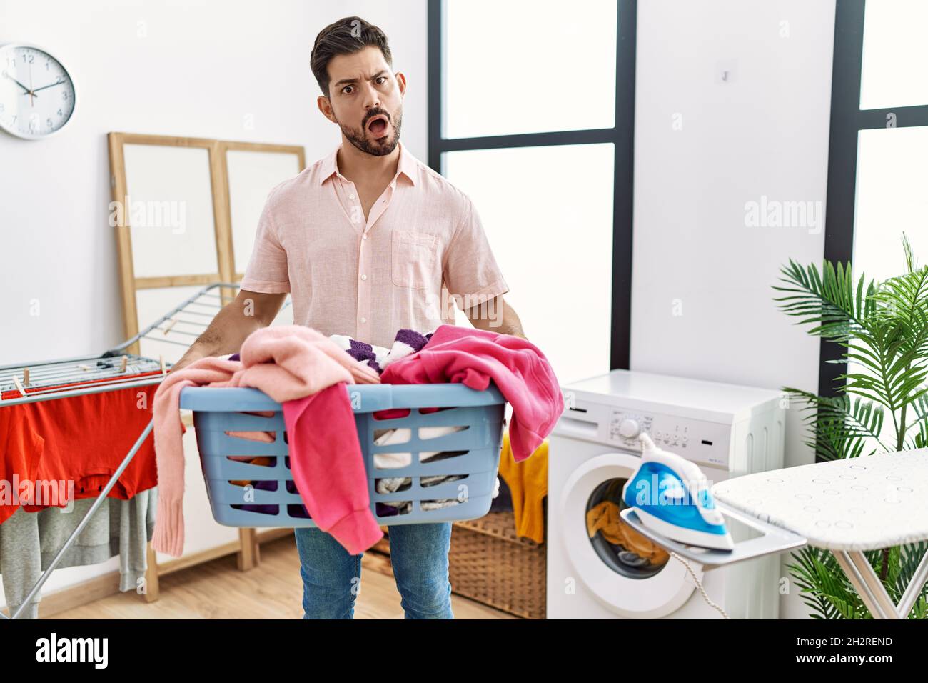 Young man with beard holding laundry basket in shock face, looking ...