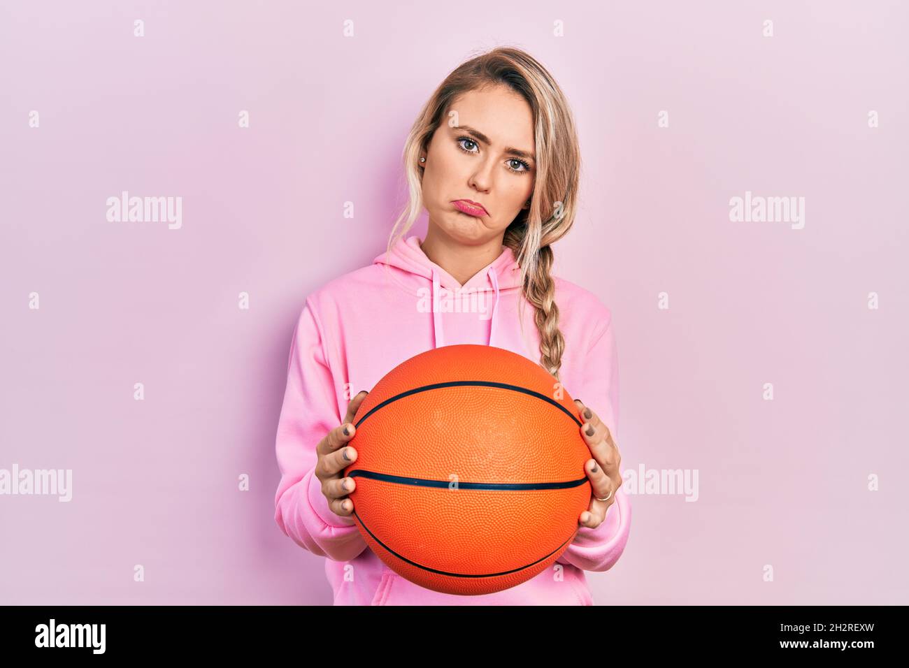 Beautiful young blonde woman holding basketball ball depressed and ...