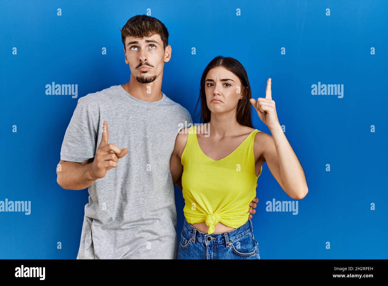 Young hispanic couple standing together over blue background pointing ...