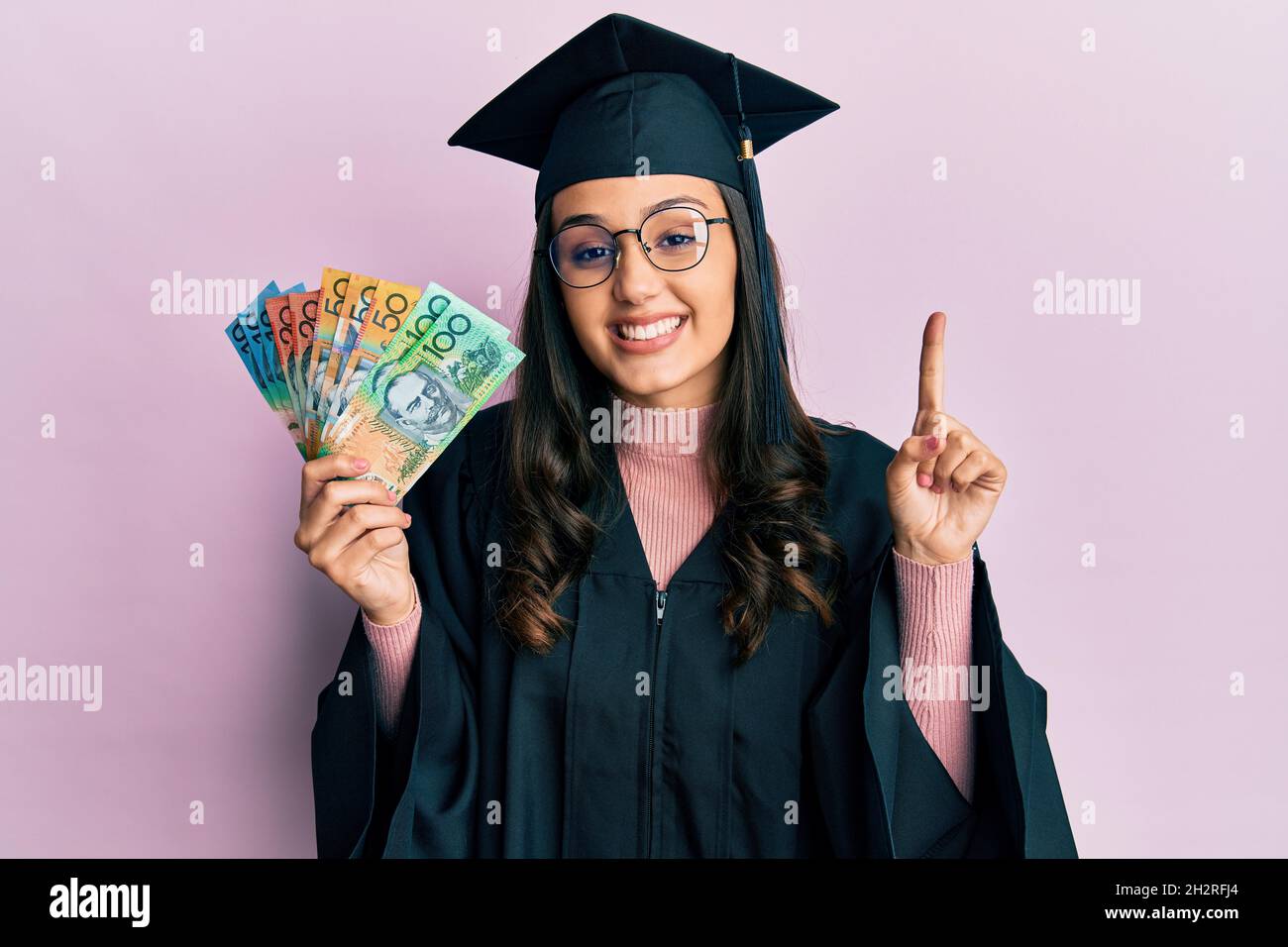 Young hispanic woman wearing graduation uniform holding australian ...