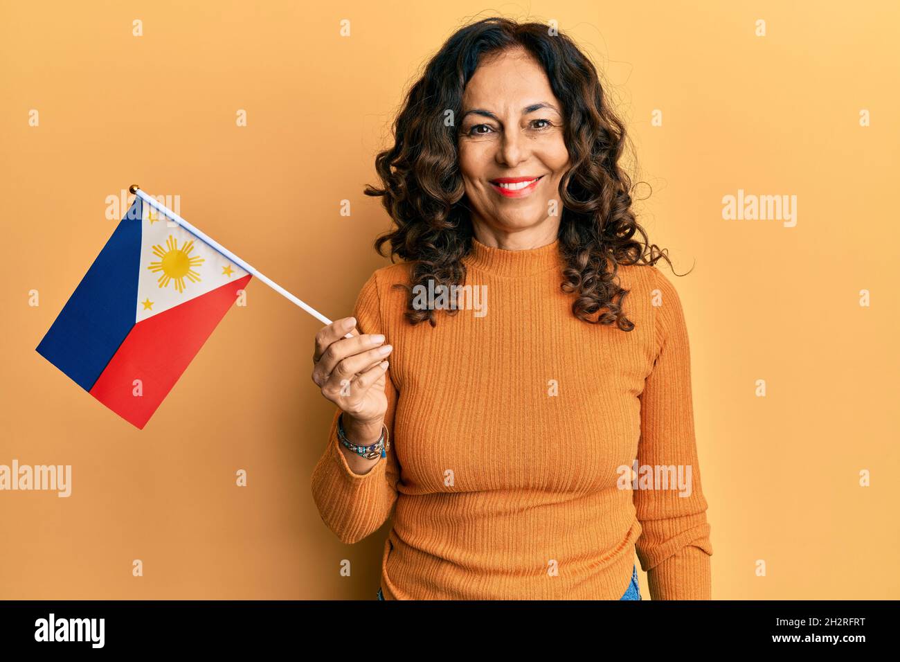 Middle age hispanic woman holding philippines flag looking positive and ...
