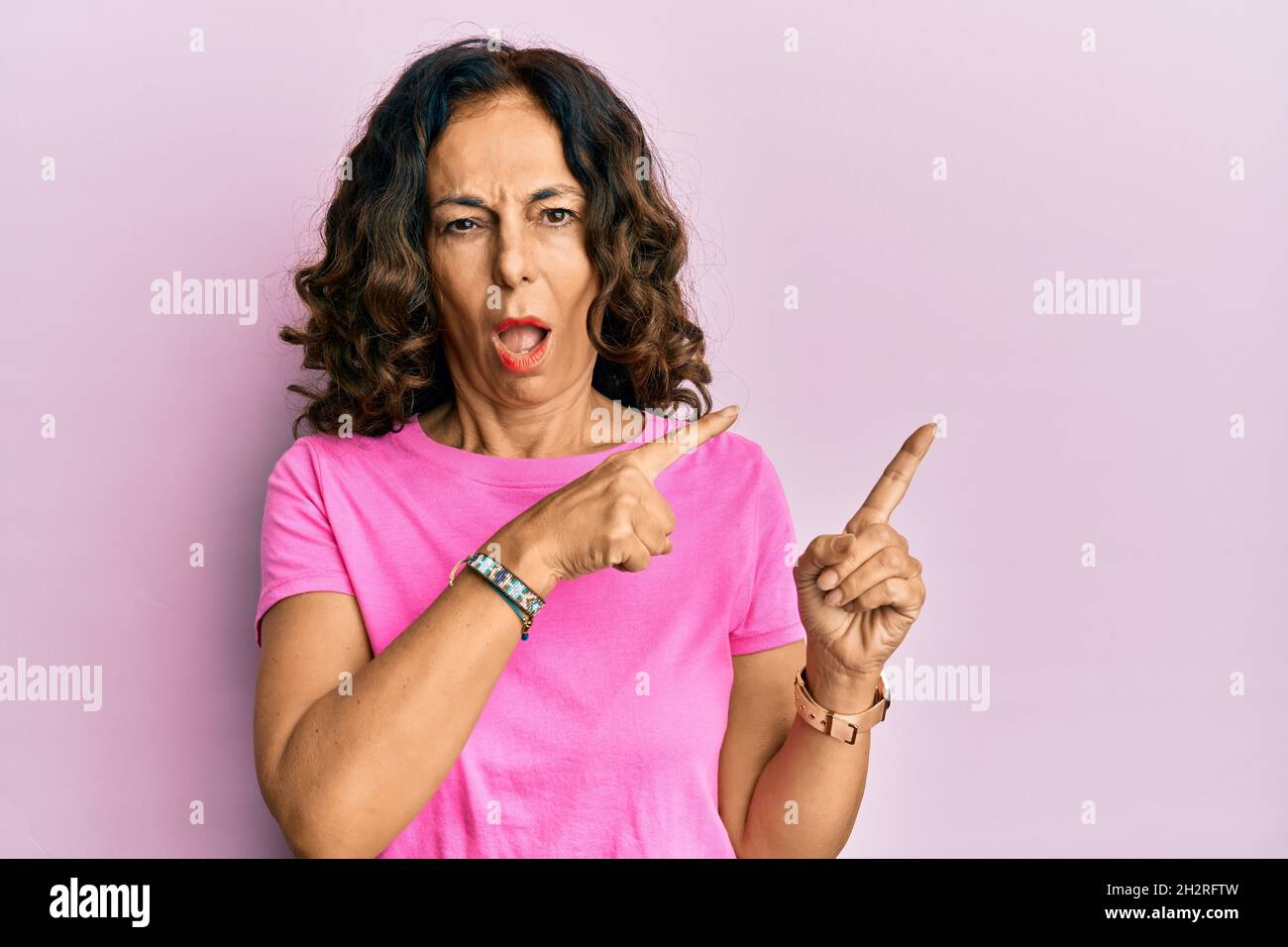Middle age hispanic woman pointing with fingers to the side in shock ...