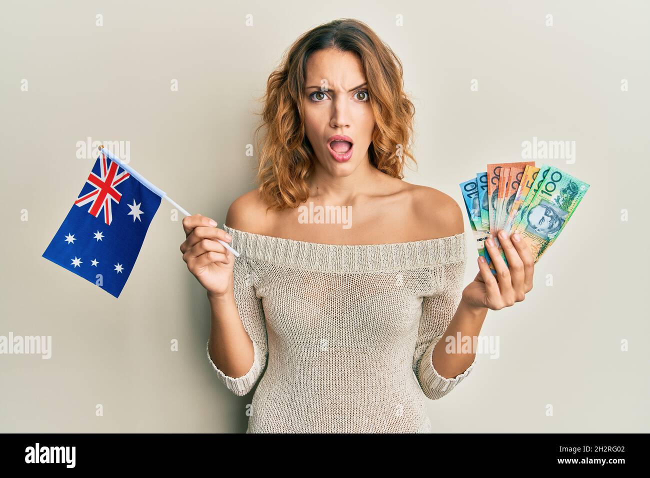 Young caucasian woman holding australian flag and dollars in shock face ...