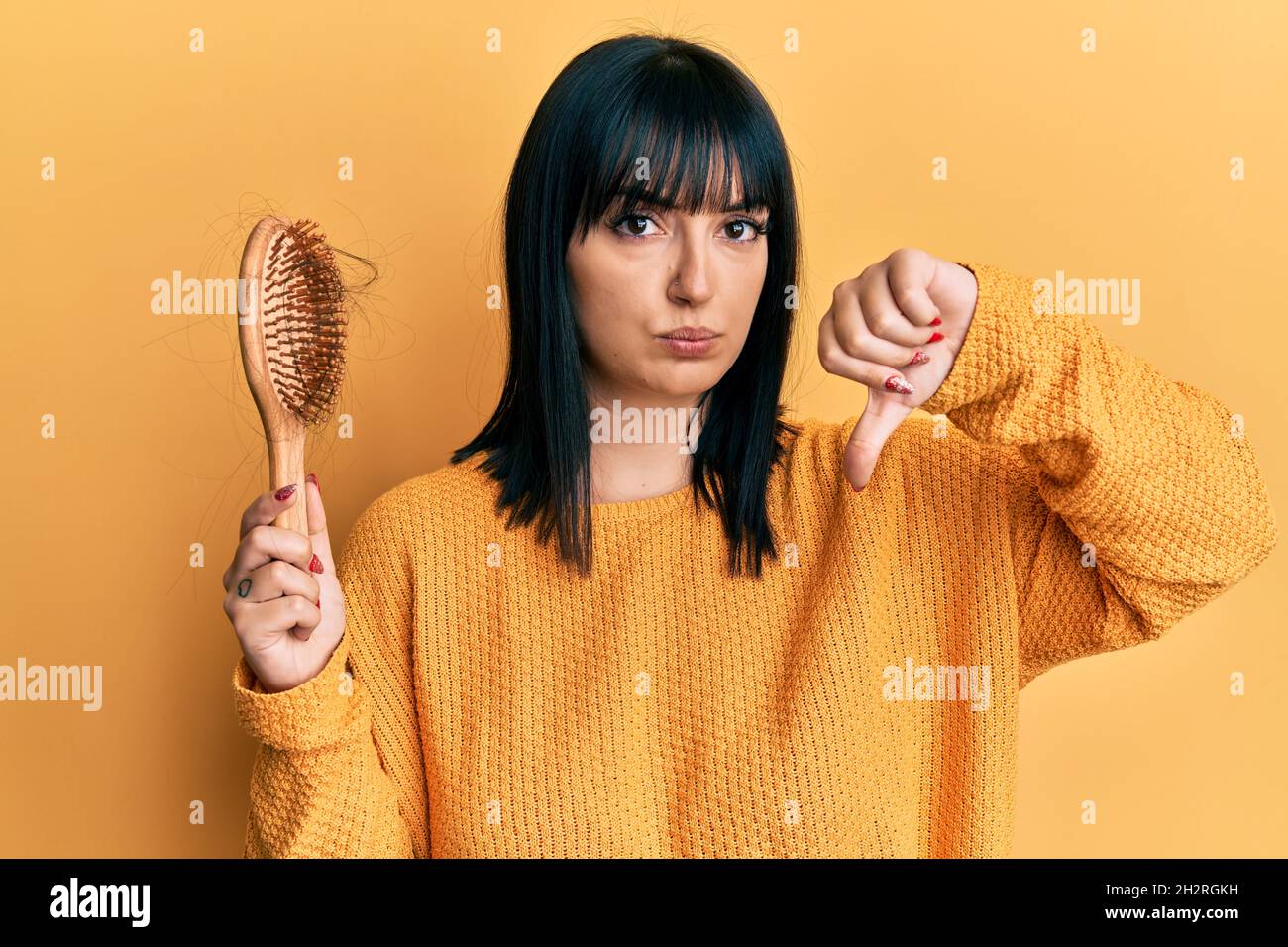 Young hispanic woman holding comb loosing hair with angry face ...
