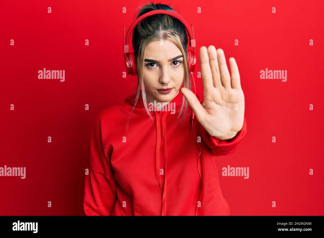 Young modern girl wearing gym clothes and using headphones doing stop ...