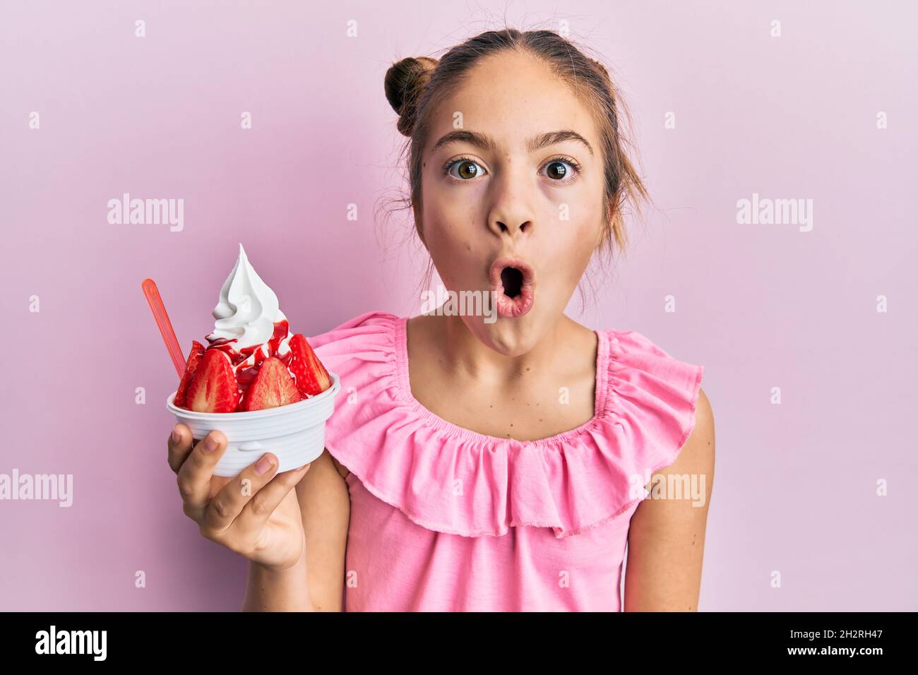 Beautiful brunette little girl eating strawberry ice cream scared and ...