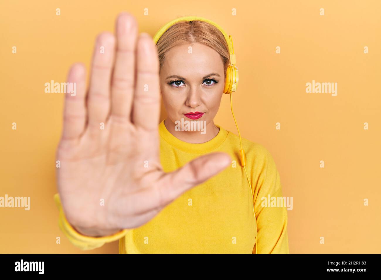 Young blonde woman listening to music using headphones doing stop sing ...