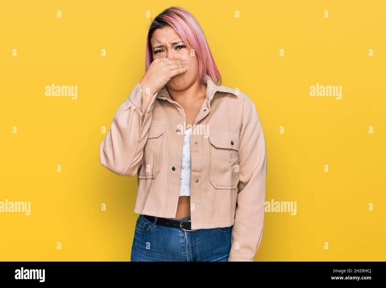 Hispanic woman with pink hair wearing casual clothes smelling something ...