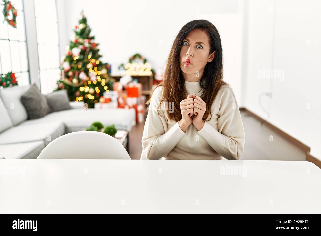 Beautiful caucasian woman sitting on the table by christmas tree making ...