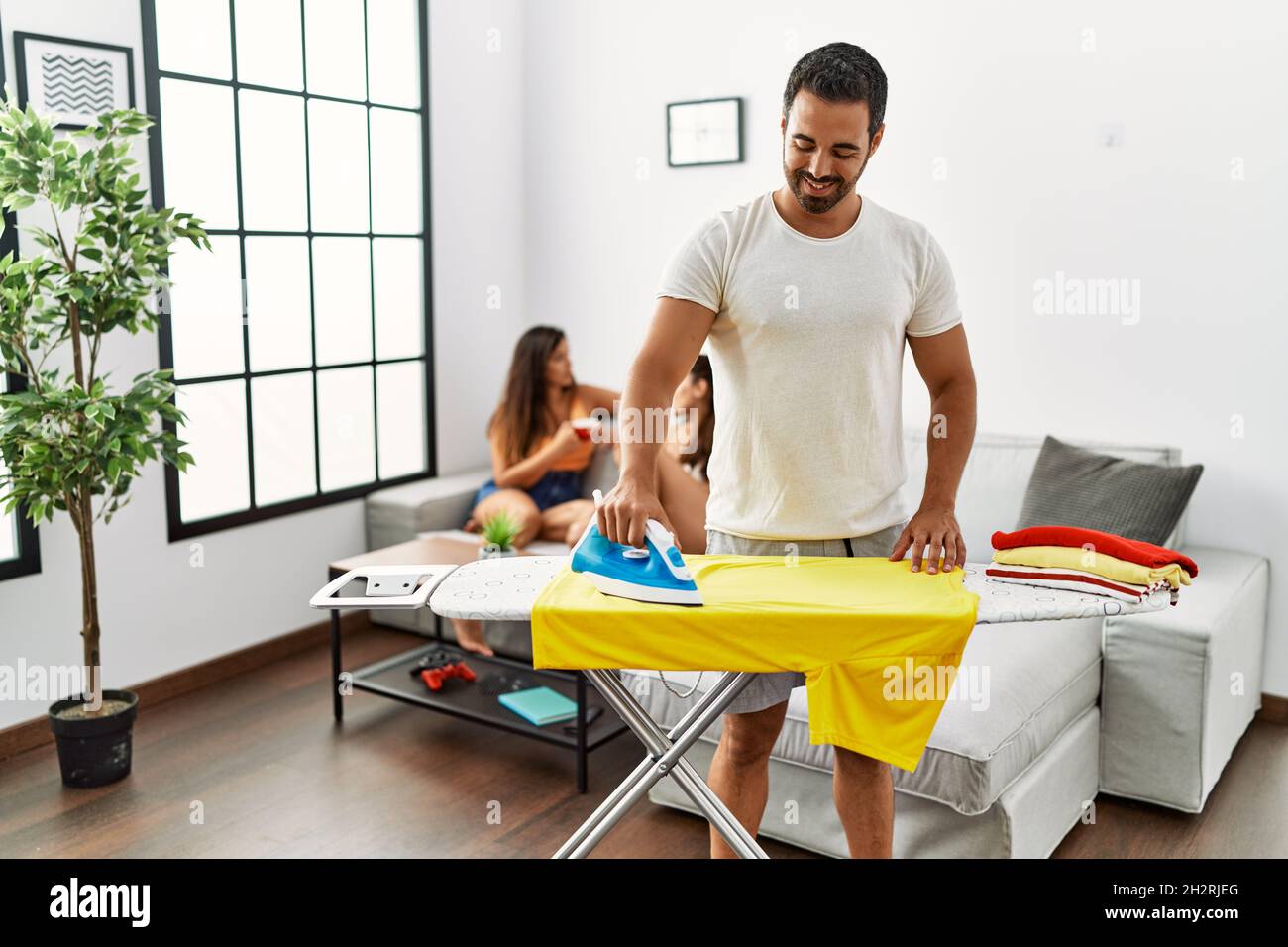Man smiling happy ironing cloths standing at living room while women ...