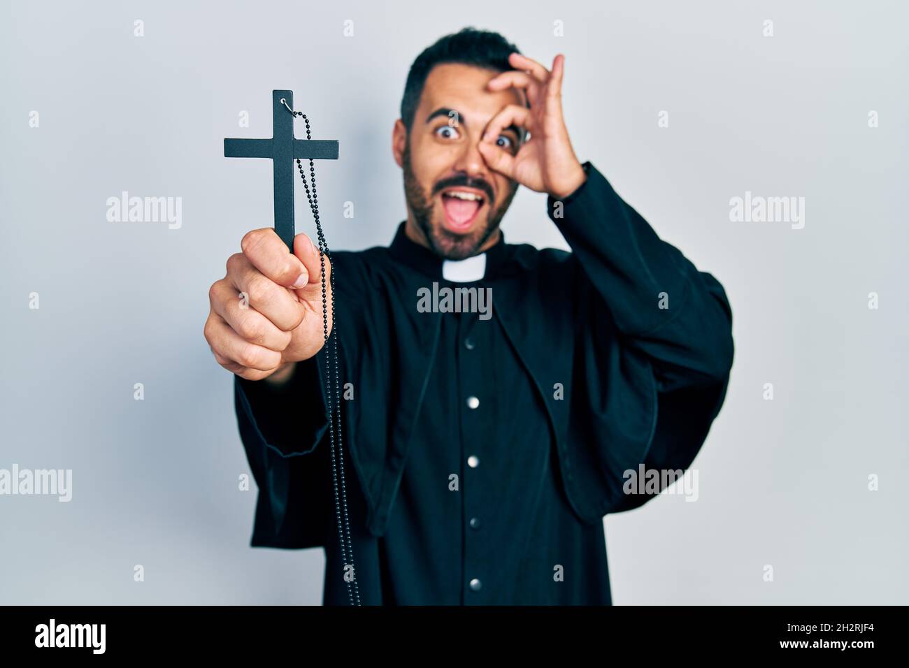 Handsome hispanic priest man with beard holding catholic cross smiling ...