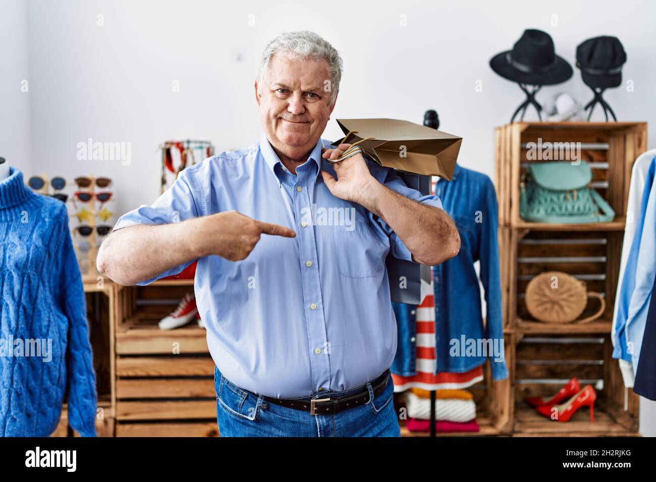 Senior man with grey hair holding shopping bags at retail shop pointing ...