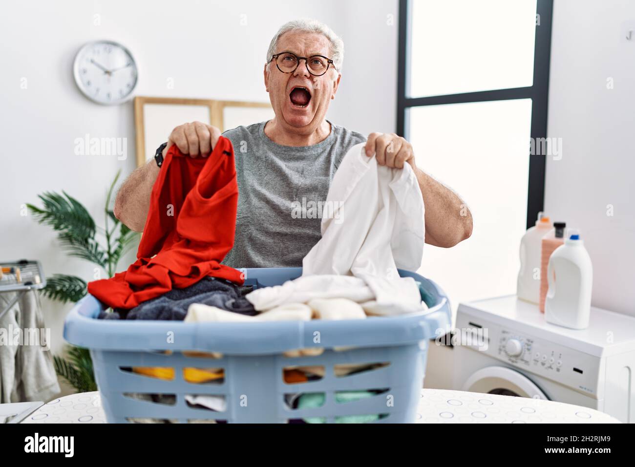 Senior caucasian man doing laundry holding clothes from wicker basket ...