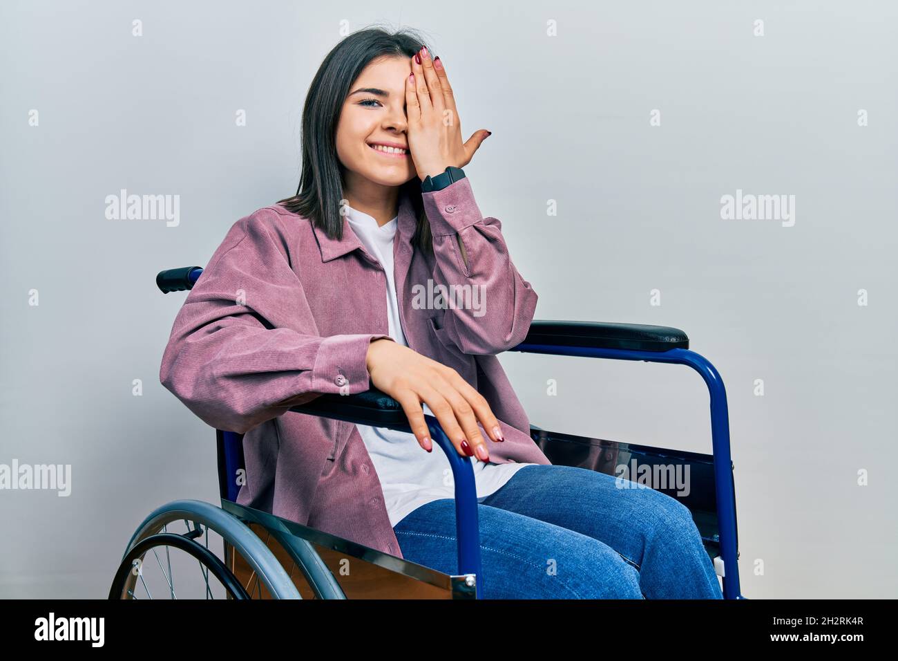Young brunette woman sitting on wheelchair covering one eye with hand ...