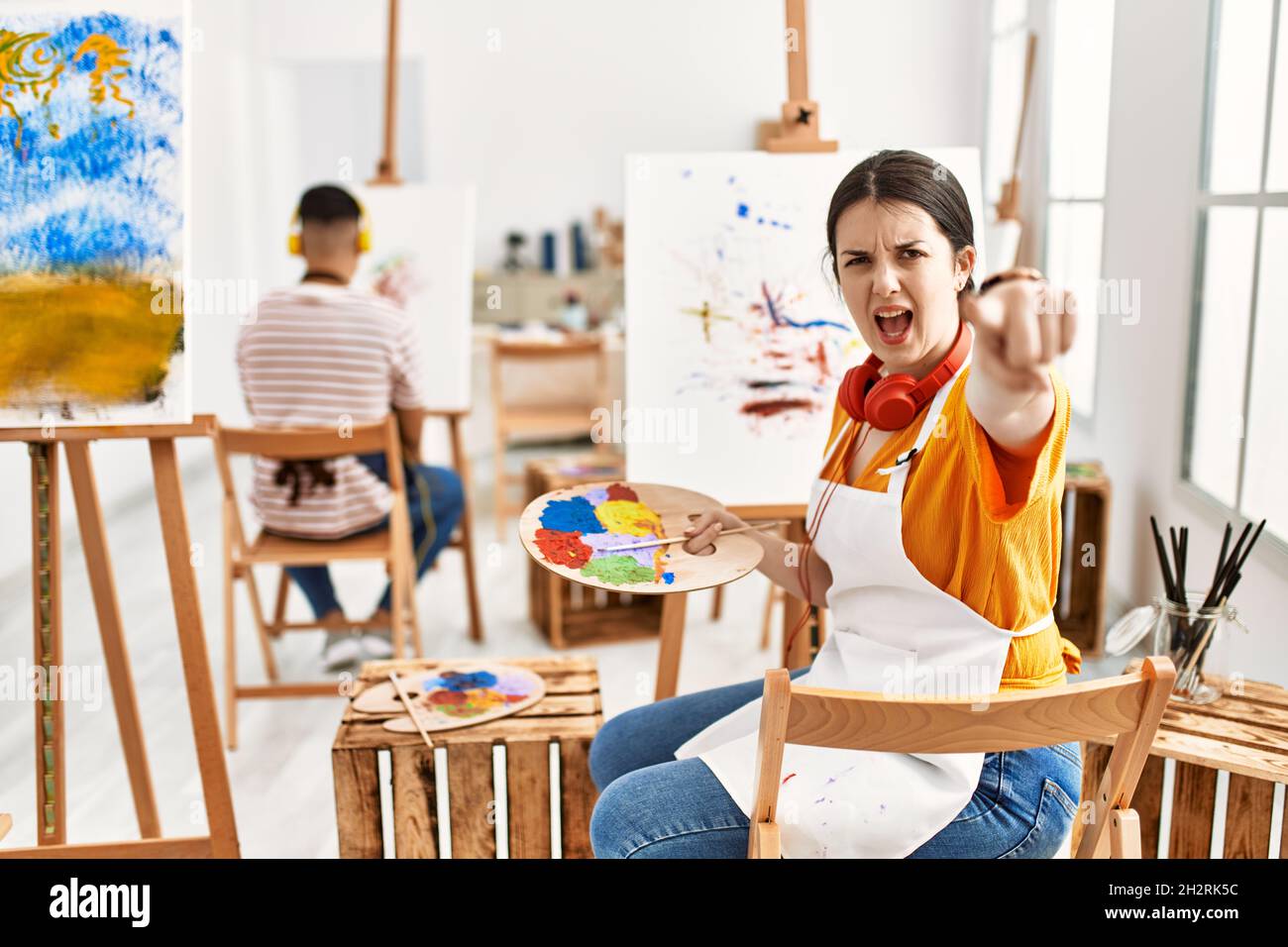 Young artist woman painting on canvas at art studio pointing displeased ...
