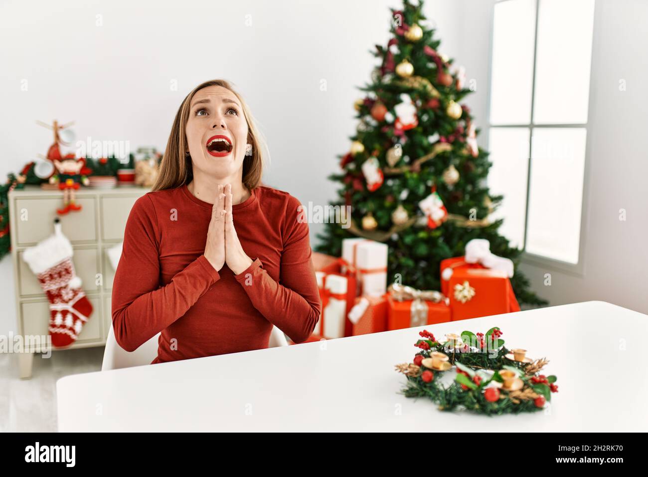 Caucasian young blonde woman sitting on the table by christmas tree ...