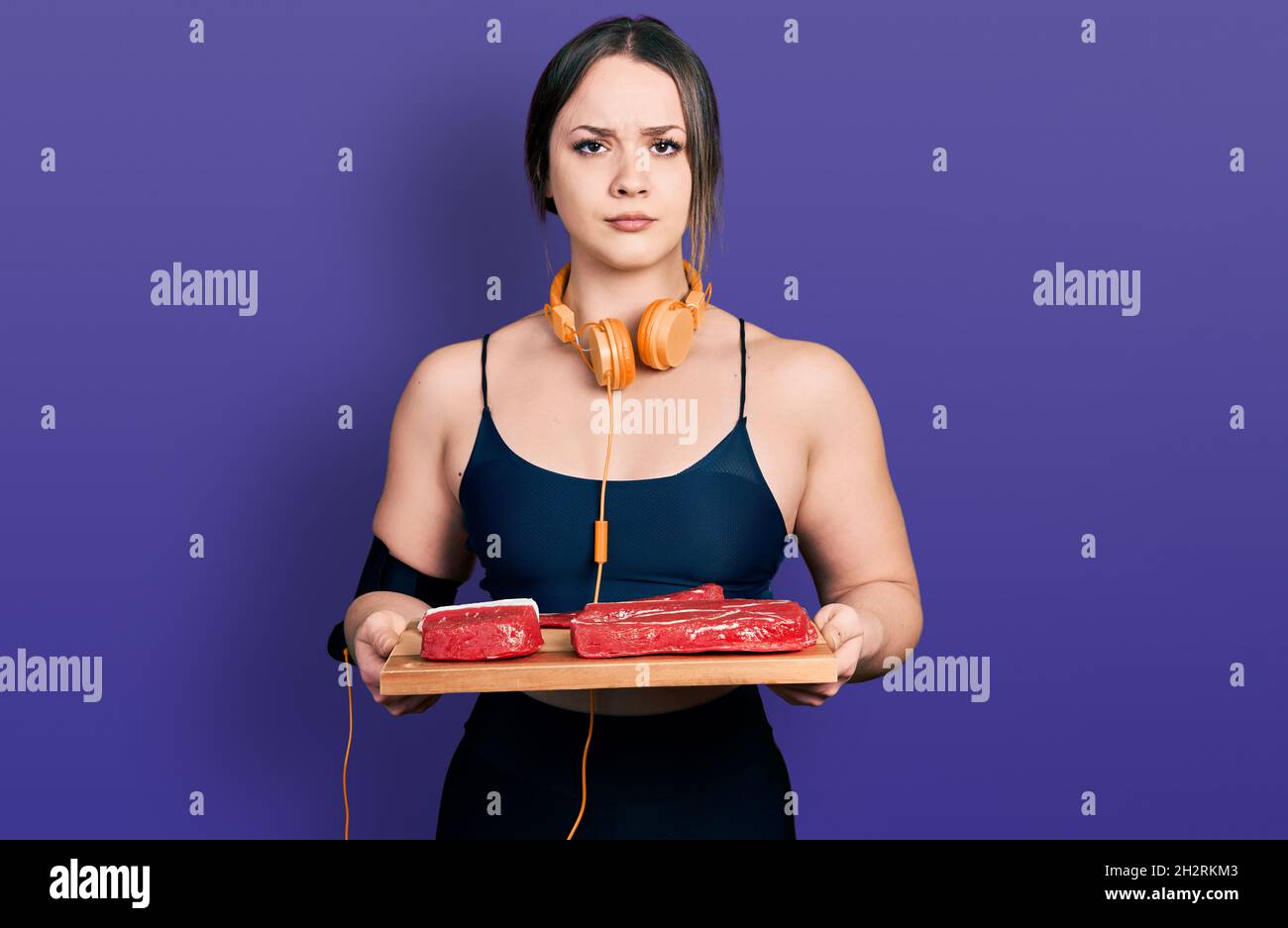 Young hispanic girl wearing workout clothes and holding meat board ...