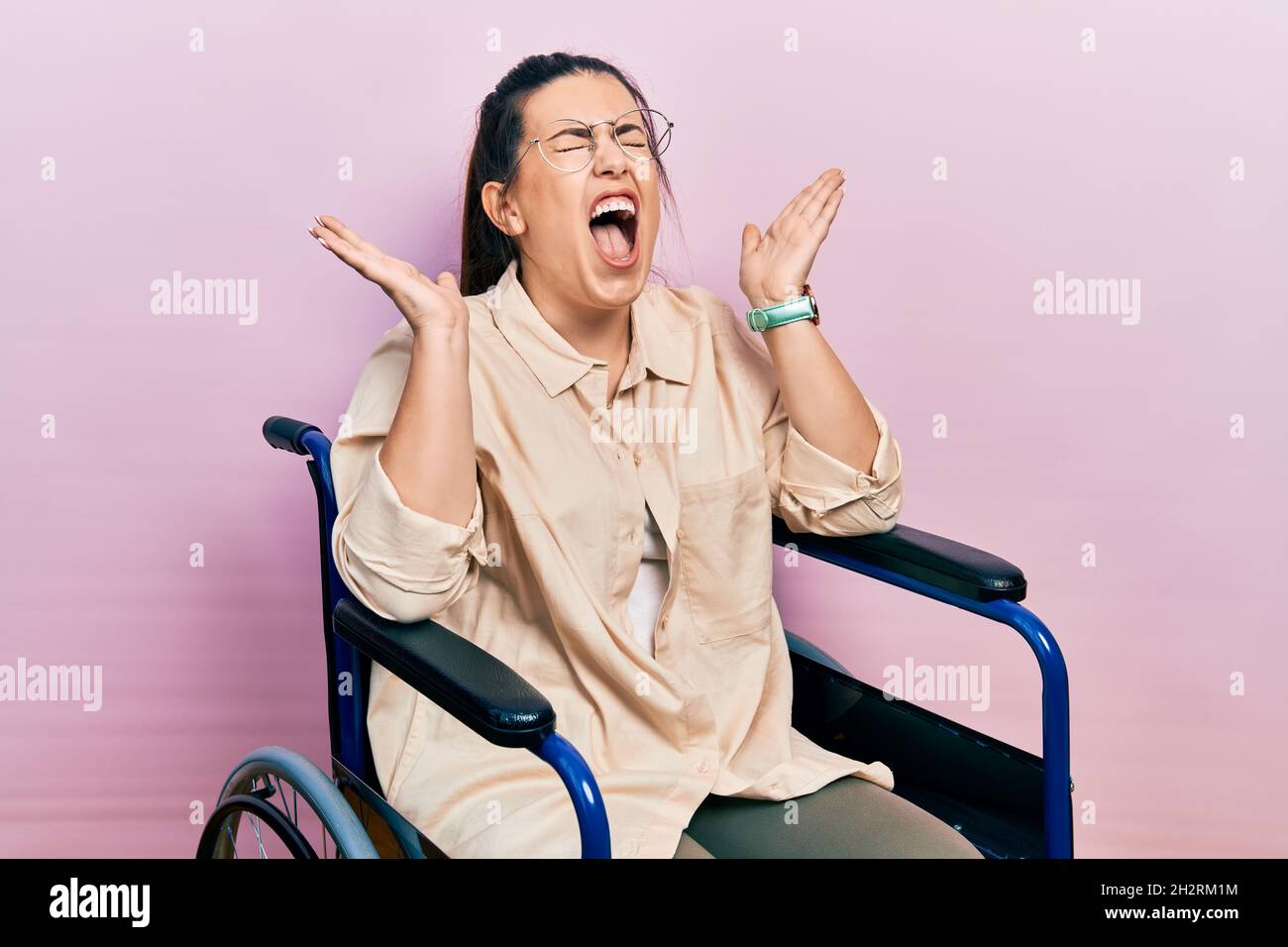 Young hispanic woman sitting on wheelchair celebrating mad and crazy ...